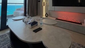 Uma sala de estar moderna com uma televisão de tela plana grande, uma lareira e vista para o oceano.