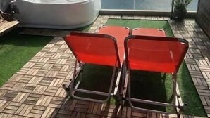 Uma varanda com vista para o mar, uma banheira de hidromassagem e duas cadeiras vermelhas.