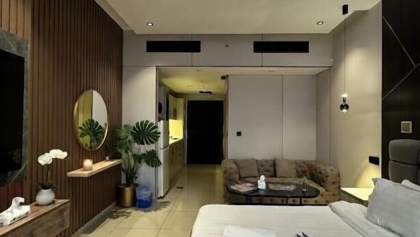 Quarto de hotel moderno com uma cama grande, área de estar e corredor que dá para outro quarto.