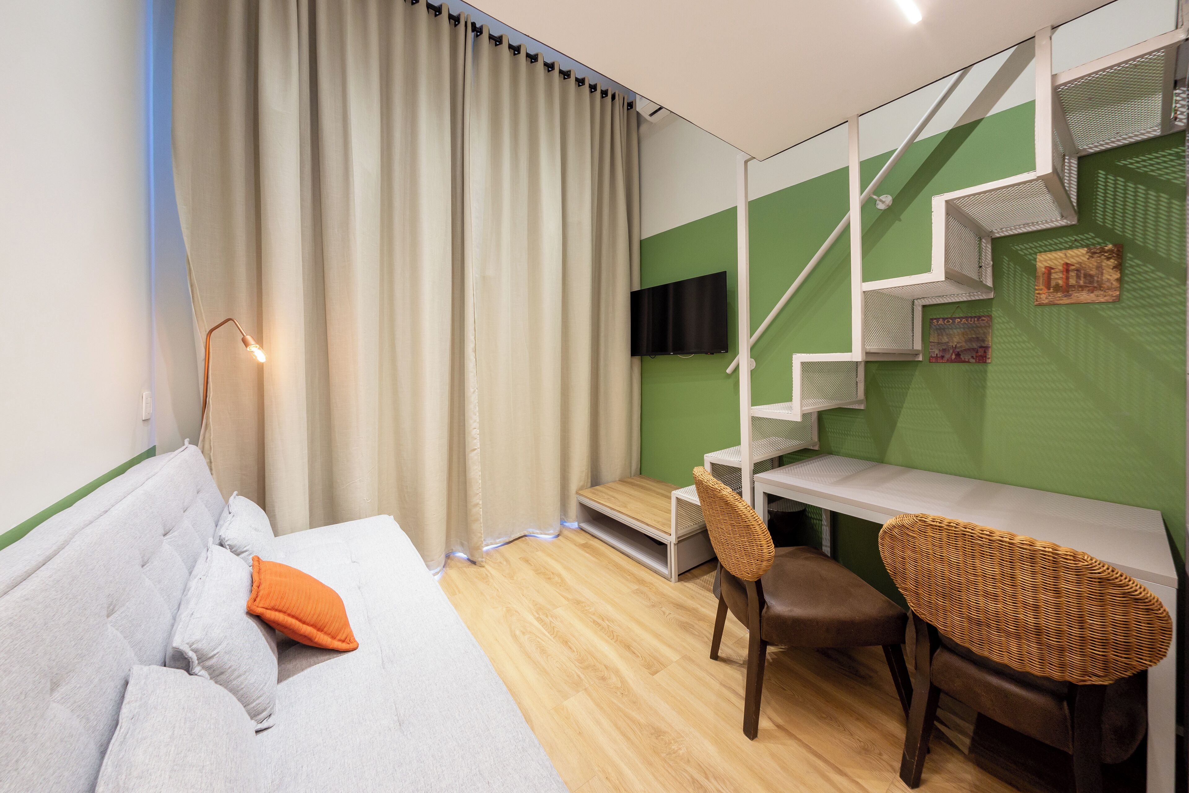 Quarto com uma cama, escrivaninha, cadeira, televisão e escada.
