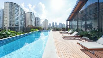 Piscina no terraço com espreguiçadeiras e vista para a cidade.