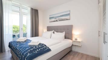 Quarto de hotel com uma cama, um quadro, uma janela com cortinas e vista para o verde lá fora.