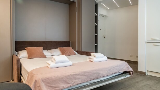 A modern bedroom with a bed, a wardrobe, and a built-in bench.