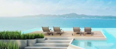 Área da piscina com espreguiçadeiras e vista para o mar.