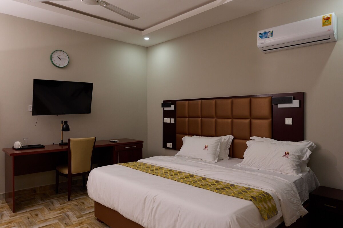 Quarto de hotel com cama, escrivaninha, cadeira, televisão e aparelho de ar condicionado.