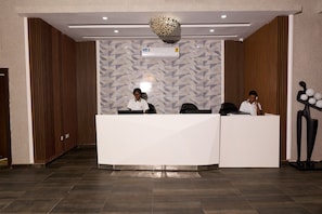 Uma área de recepção com design moderno, destacando um balcão de atendimento, uma parede decorativa e um aparelho de ar condicionado instalado no teto.
