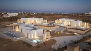 A modern villa complex with multiple buildings, outdoor pools, and a desert landscape in the background.