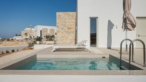 A modern outdoor pool area with a stone wall, a lounge chair, and a door leading to a building.