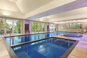 Uma grande piscina interior com paredes de vidro transparente, uma banheira de hidromassagem e um relógio na parede.