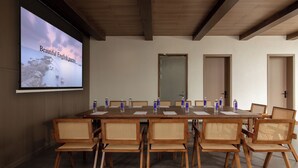 Uma sala de conferências com uma mesa comprida, cadeiras, uma tela de projetor e portas.