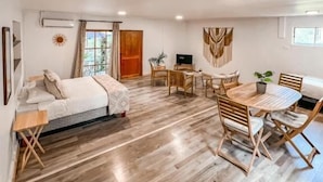 Um quarto espaçoso com piso de madeira, uma cama, uma mesa de jantar com cadeiras e uma televisão.