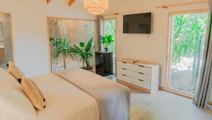 Quarto com cama, mesa de cabeceira, televisão e uma janela grande com vista para o verde.
