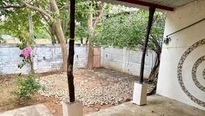 Uma área externa coberta com piso de concreto, parede de tijolos e uma árvore.