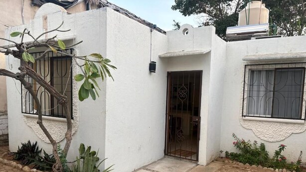 Um edifício de paredes brancas com portão e uma pequena área de jardim com plantas, e um reservatório de água visível no telhado.