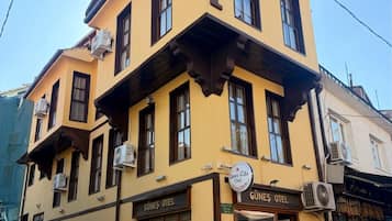 Um hotel de dois andares com fachada amarela, várias janelas e um aparelho de ar condicionado na parte externa.