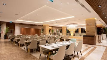 Ampla área de jantar com várias mesas e cadeiras, um lustre central e design moderno no teto.