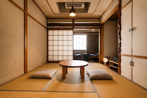 Um quarto japonês tradicional com tatames, uma mesa baixa, almofadas, portas deslizantes e vista para o exterior.