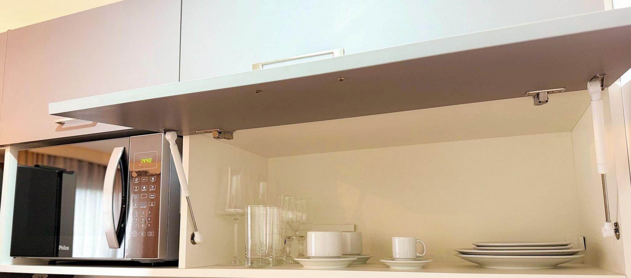 Uma cozinha compacta com micro-ondas, cafeteira e um pequeno espaço de refeições com alguns pratos e copos.
