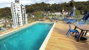 Piscina no terraço com vista para uma área residencial e um prédio alto ao fundo.