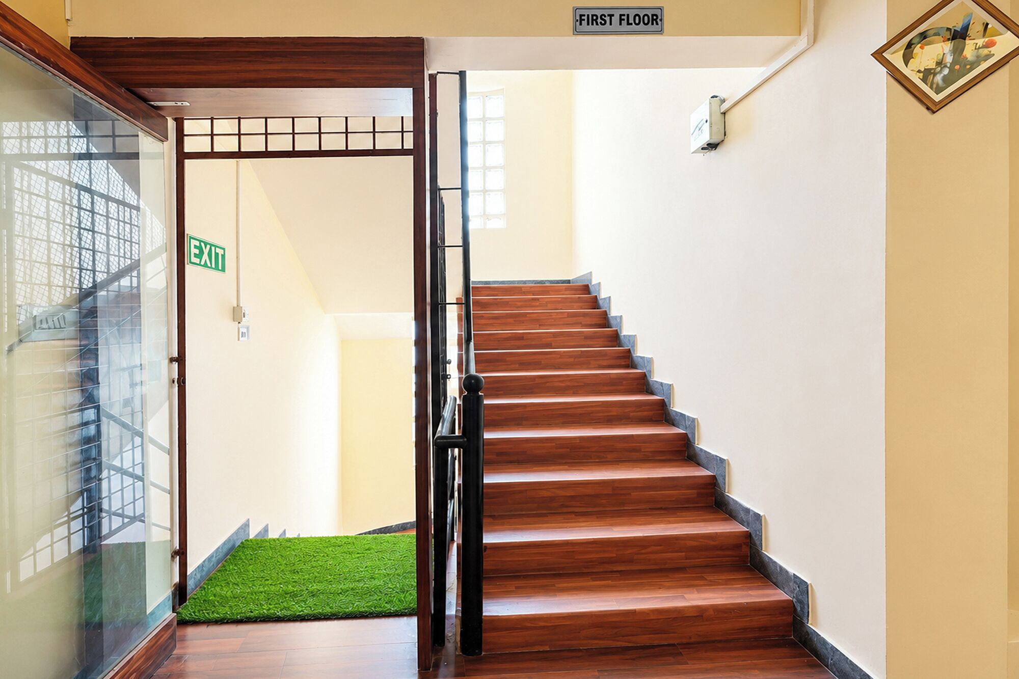 Escadaria que leva ao primeiro andar, com uma porta de vidro à esquerda e um tapete verde na base.