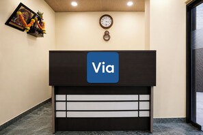 Bancada de recepção com uma placa que diz 'Via' e um relógio acima.
