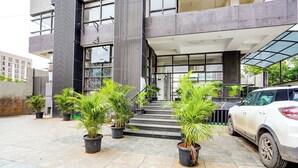 Entrada de hotel com design moderno, destacando uma escadaria que leva à entrada, plantas em vasos e um carro estacionado.