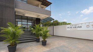 Entrada de um hotel moderno com uma placa indicando 'PUNE GRAND ROOMS' e um céu claro.