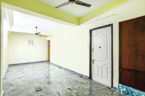 Um corredor com piso de mármore, ventilador de teto, uma porta branca e uma porta de madeira.