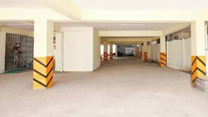 Um corredor com piso ladrilhado, paredes brancas e pilares listrados em laranja e preto.