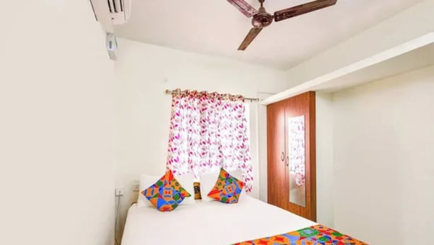 Quarto com cama, almofadas, ventilador de teto e janela com cortinas.