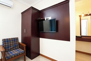 Um quarto com um guarda-roupa, uma televisão presa na parede e uma cadeira de padrão xadrez.