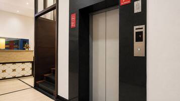 Um elevador com visor digital, placa de 'Proibido Fumar' e sinal de segurança contra incêndio.