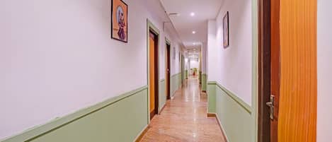 Corredor de hotel com portas em ambos os lados, piso de mármore e quadros nas paredes.