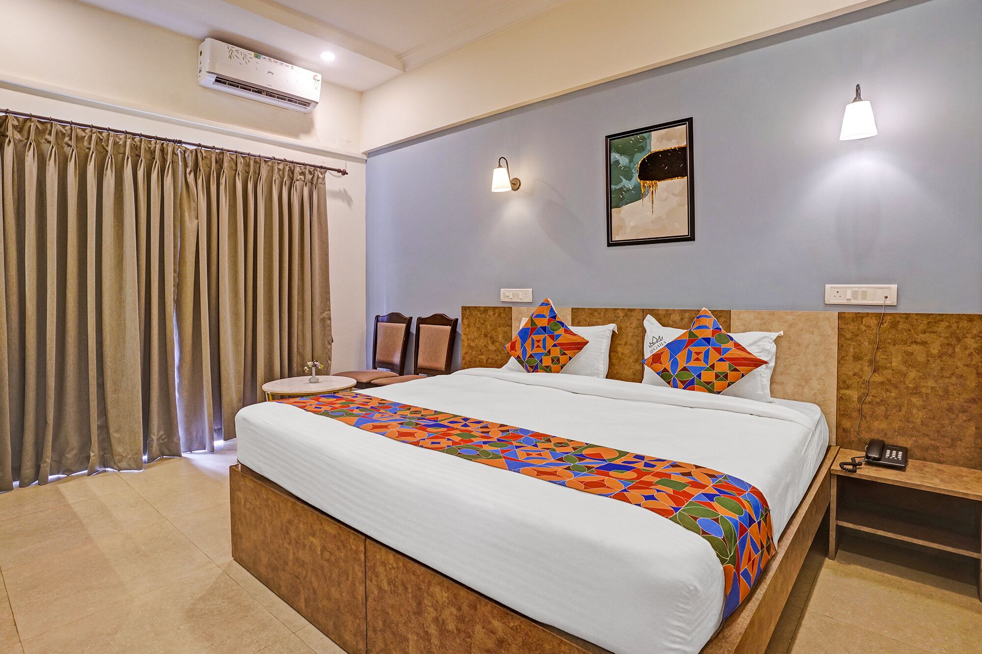 Quarto de hotel com uma cama grande, mesa de cabeceira, uma cadeira, ar condicionado fixado na parede e uma janela com cortinas.