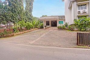 Edifício com entrada pavimentada, rodeado por vegetação e cercado por uma grade de metal.