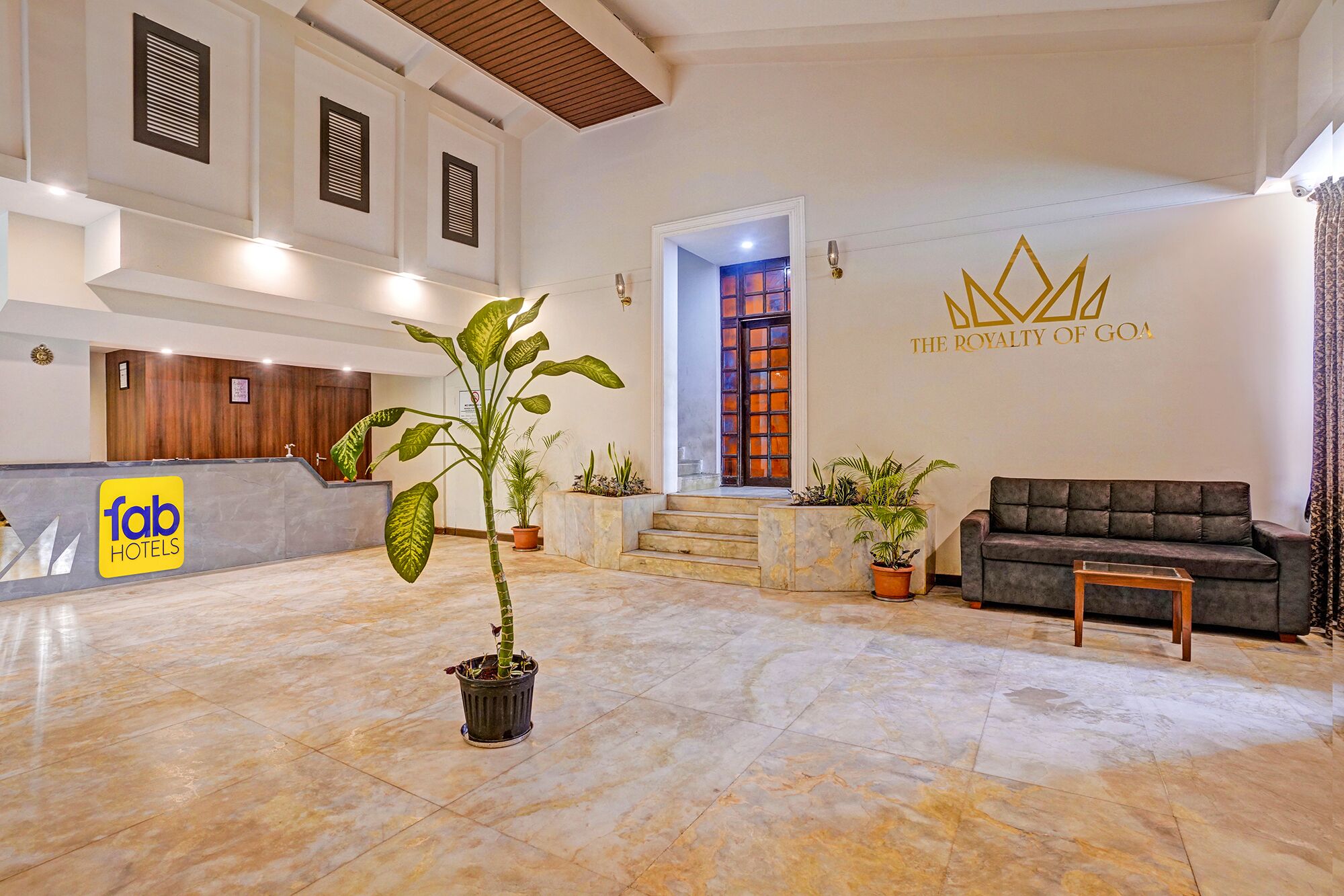 Um hall de hotel com um balcão de recepção, uma planta em vaso, um sofá e uma parede com um logotipo.