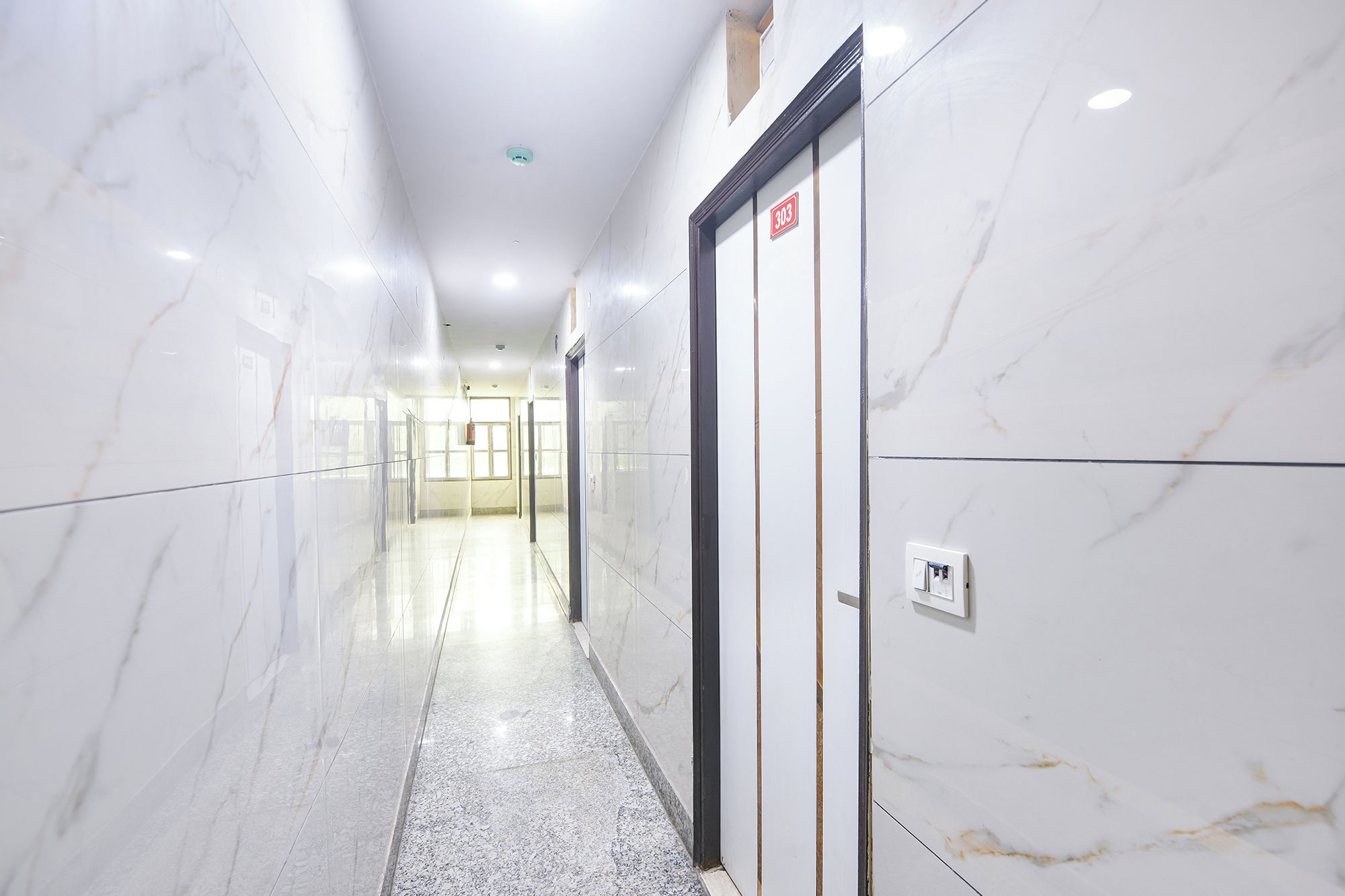 Corredor com paredes e piso de mármore, que leva a um elevador com placa indicando o número do andar.