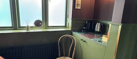 Uma cozinha pequena com janela, uma cadeira e um radiador.
