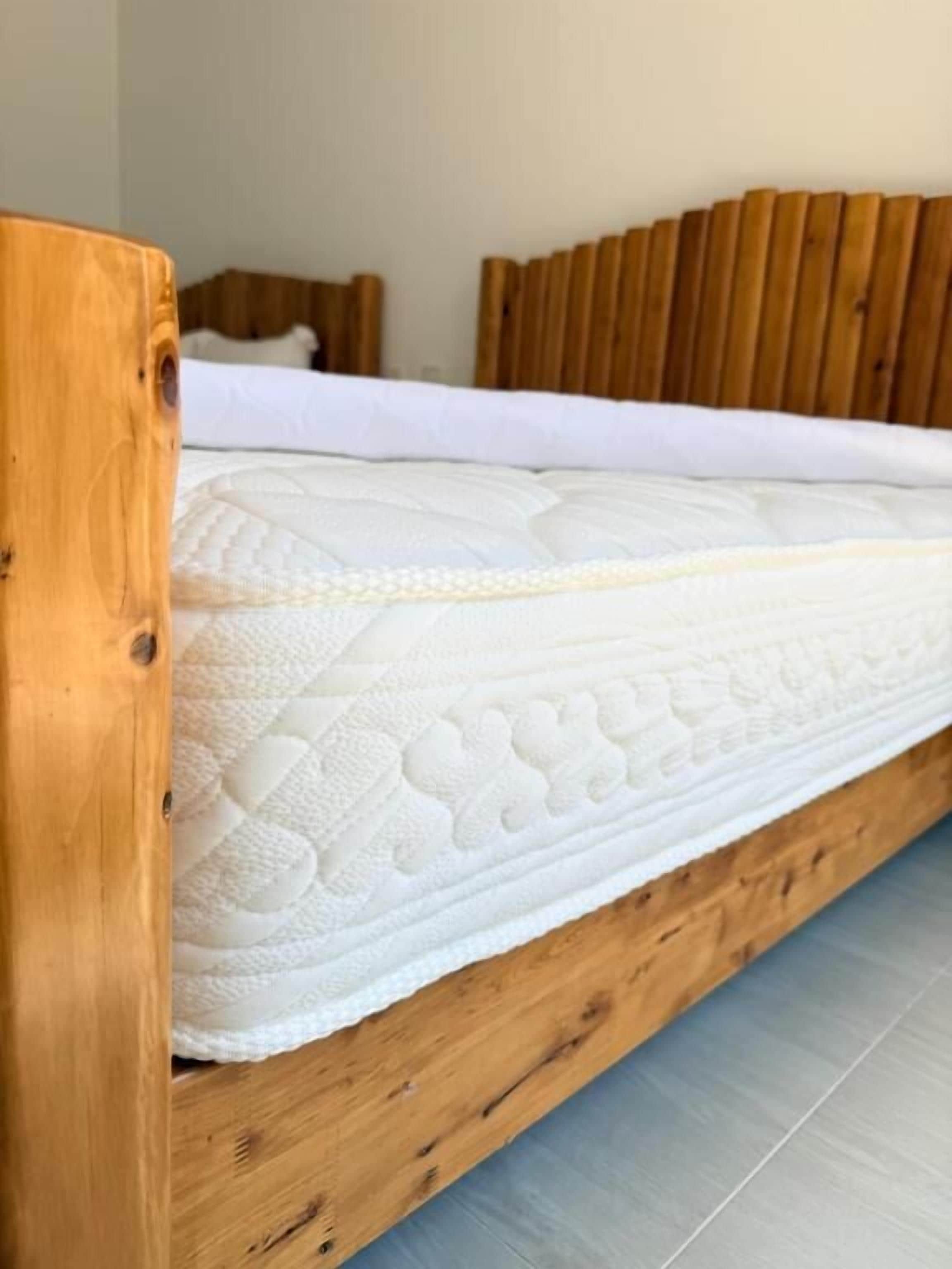 Uma cama com estrutura de madeira, colchão branco e cabeceira de madeira.