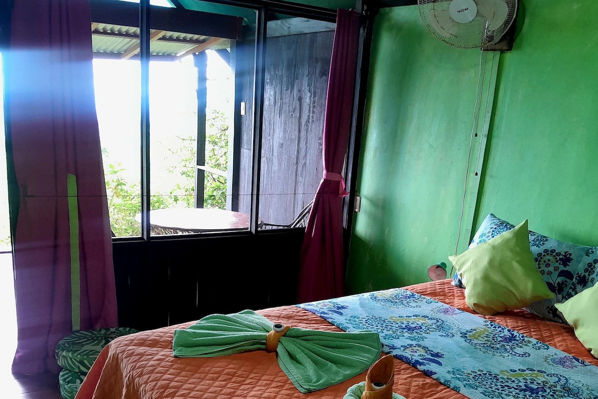Quarto com cama, ventoinha e janela com cortinas.