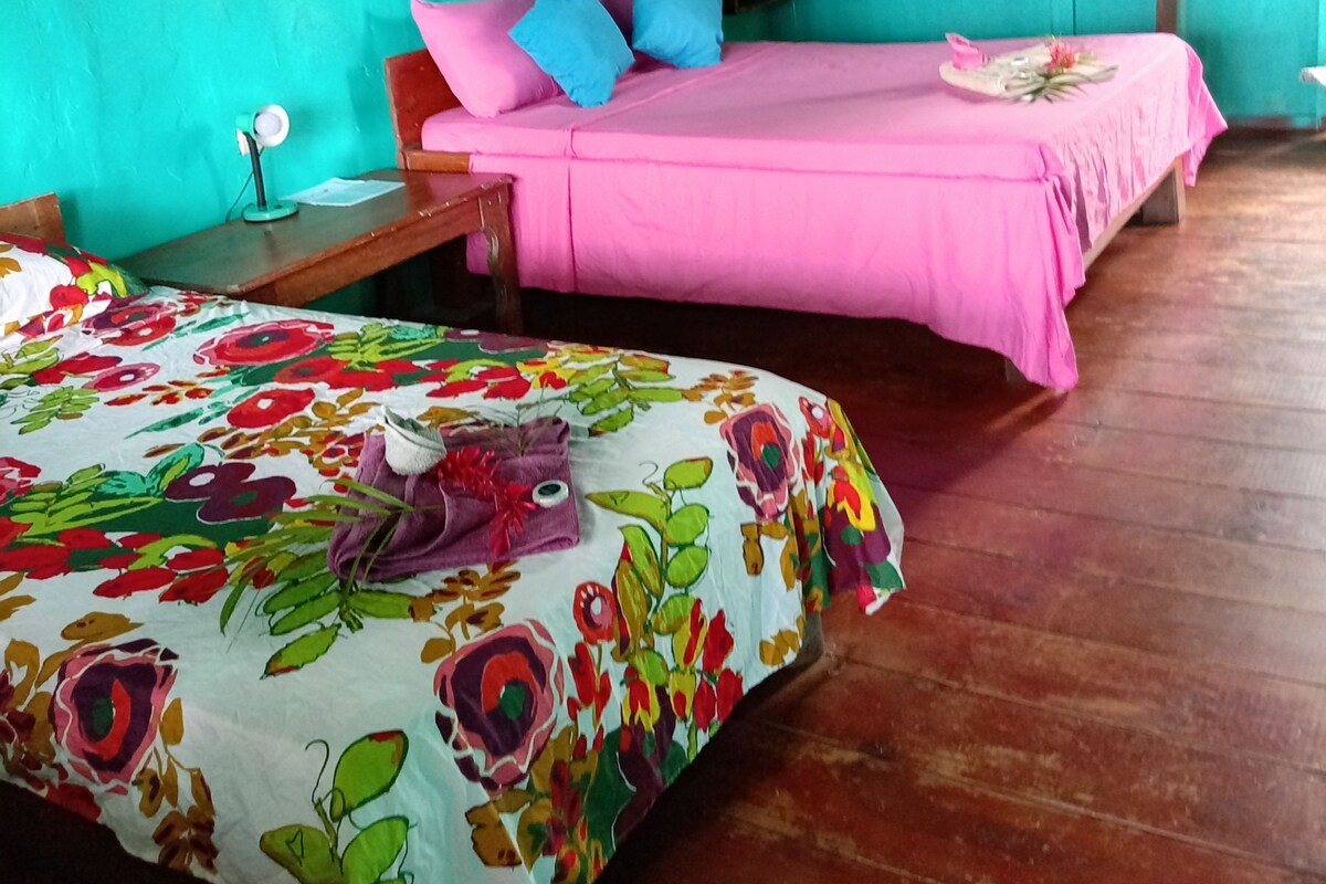 Quarto com duas camas, uma com colcha florida e a outra com colcha rosa.