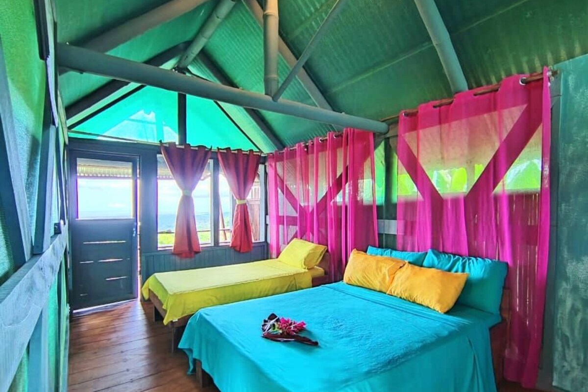 Quarto com duas camas, piso de madeira e telhado de metal verde.