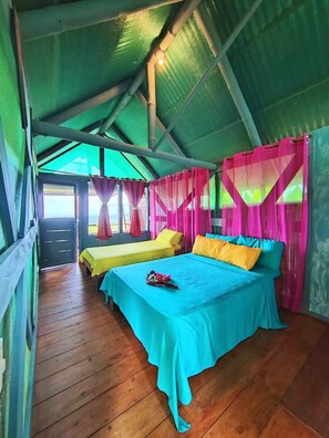Quarto com duas camas, piso de madeira e telhado de metal verde.