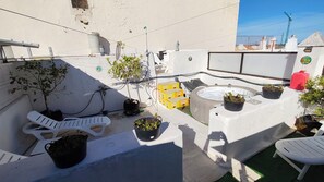 Terraço no telhado com cadeiras de plástico branco, plantas em vasos e uma pequena piscina.