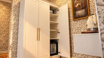 Quarto com guarda-roupa branco, quadro na parede e um pequeno armário com abajur.