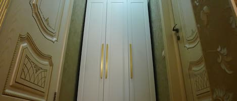 Um guarda-roupa branco com duas puxadores, ladeado por molduras decorativas e uma parede estampada.