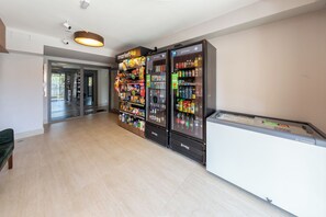 Corredor com máquina de vendas abastecida com lanches e bebidas, um banco e uma área de recepção com balcão.