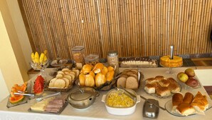 Uma mesa de buffet com diversos alimentos, incluindo pão, doces, frutas e um bolo.