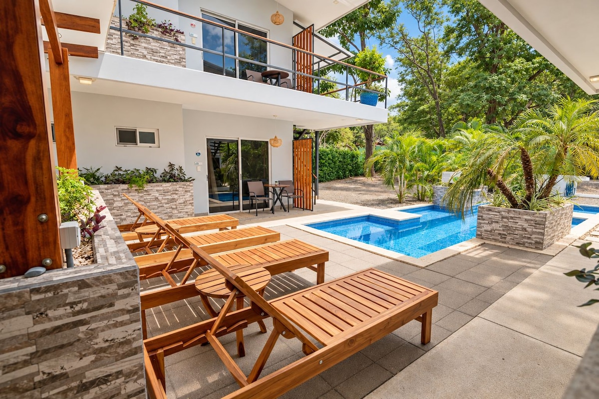 Uma casa moderna de dois andares com piscina, deck de madeira e área de estar externa.