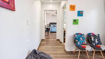 Corredor que dá para um quarto com uma cama, uma cadeira com almofadas coloridas e obras de arte nas paredes.